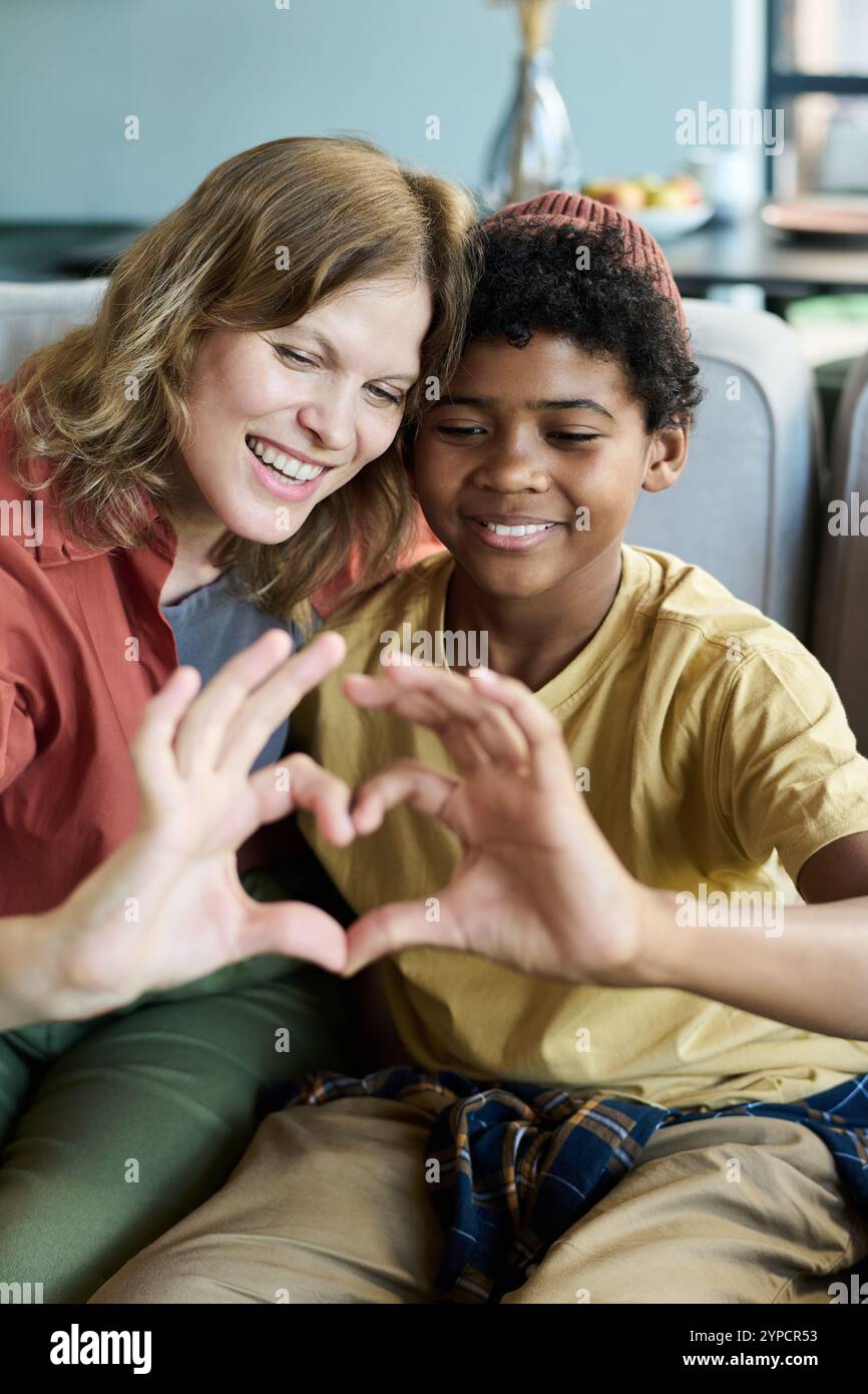 Mother and son forming heart shape gesture with hands while sitting on ...