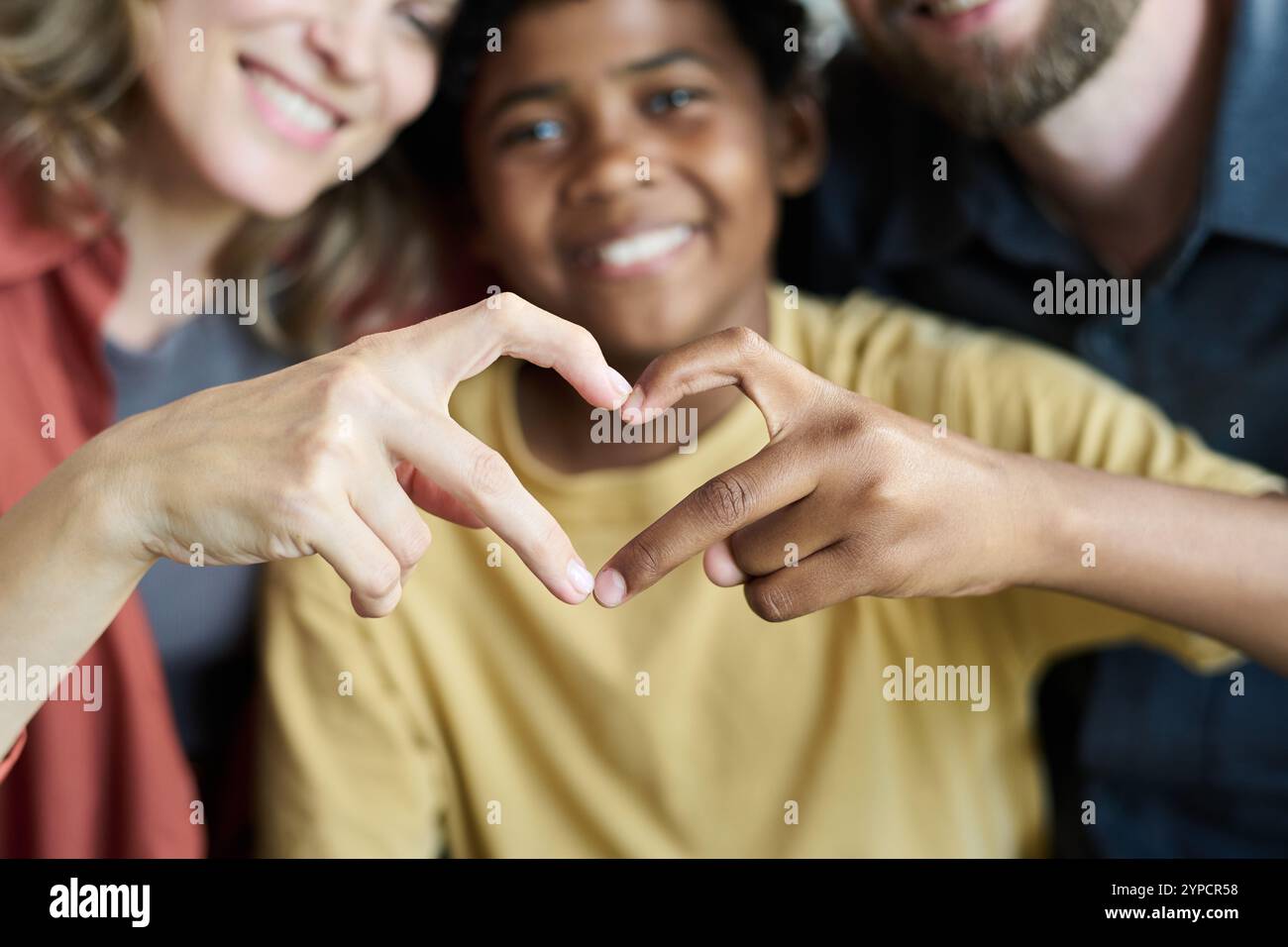 Biracial child playing with two adults and making heart shape gestures ...