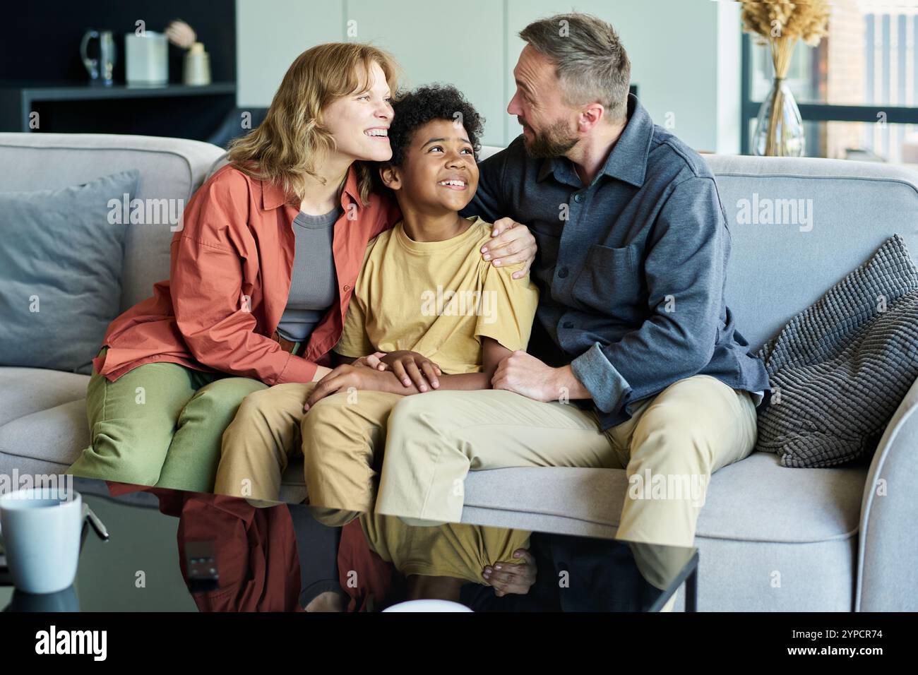 Group of three family members sitting together on couch smiling and ...