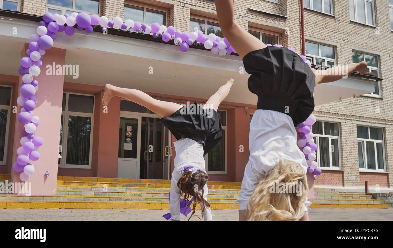 Two happy schoolgirls doing cartwheels in front of their school on the ...