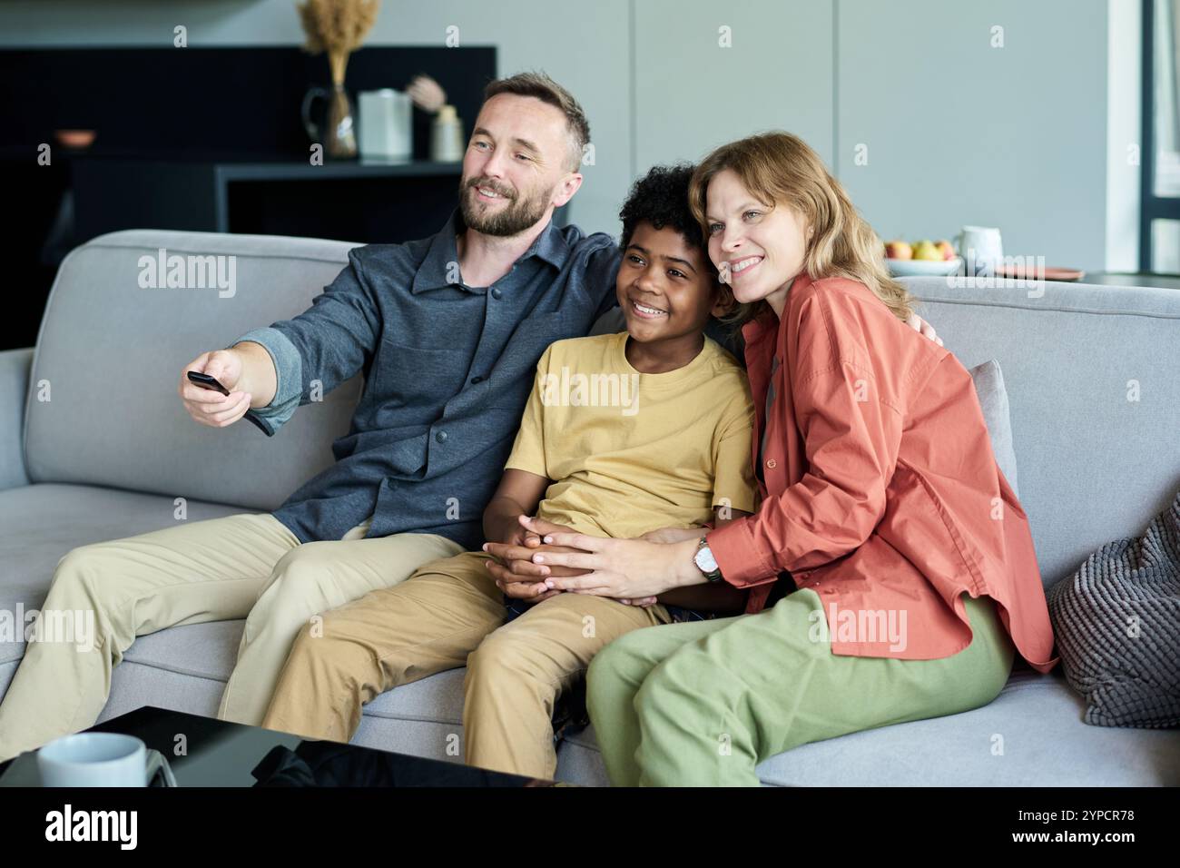 Smiling family sitting on a modern sofa in bright living room, holding ...