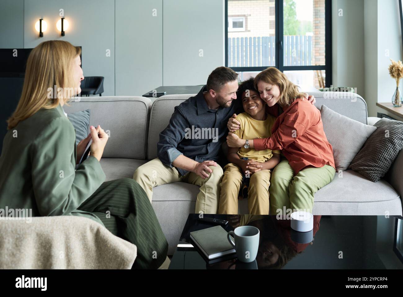 Family gathered on living room sofa with two parents embracing their ...