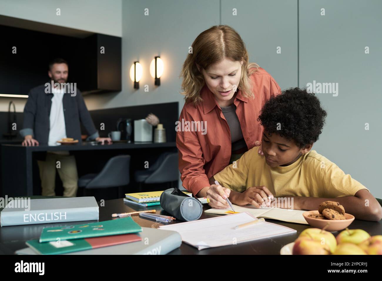 Adult assisting child with homework while another person observes from ...