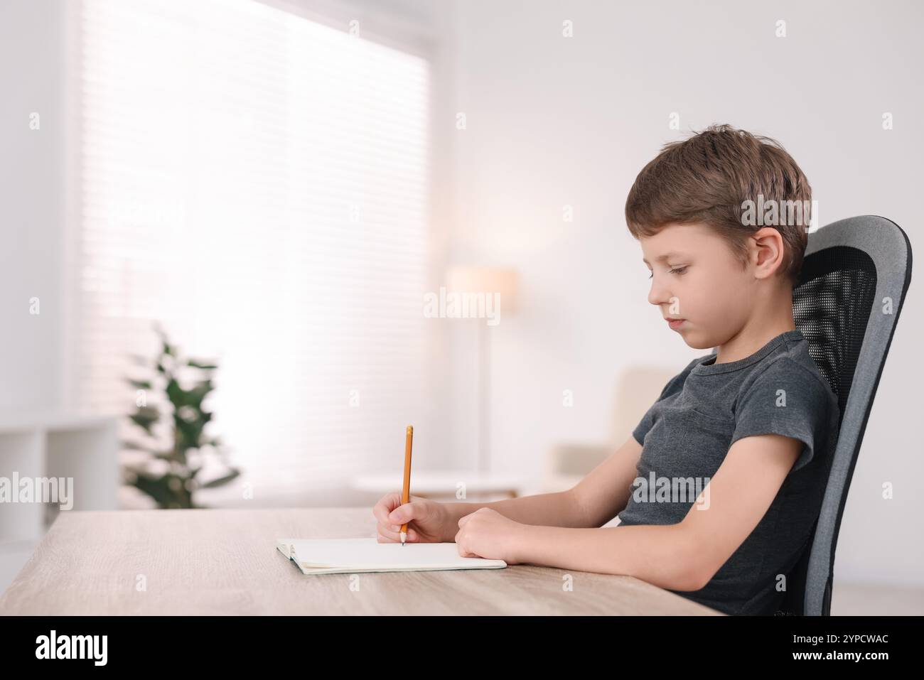 Boy with correct posture doing homework at wooden desk indoors Stock ...