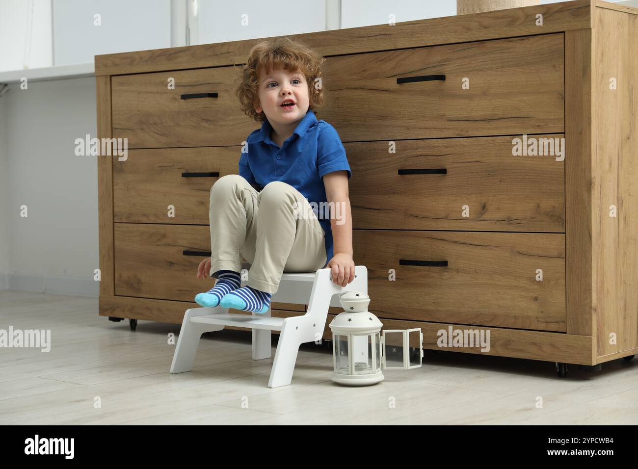 Little boy sitting on step stool near chest of drawers at home Stock ...