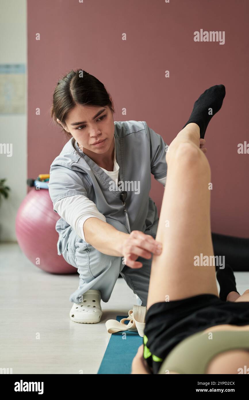 Physical therapist assisting patient with leg stretching exercise in ...
