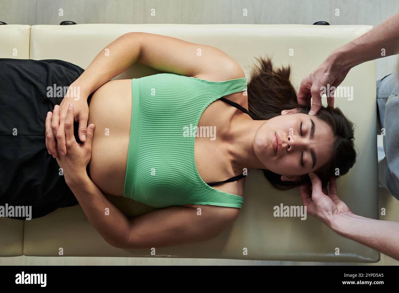 Woman lying on treatment table, receiving chiropractic adjustment on neck. Therapist's hands ...