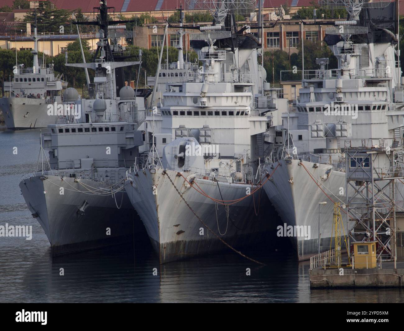 Three large military ships side by side in an industrial harbour area ...