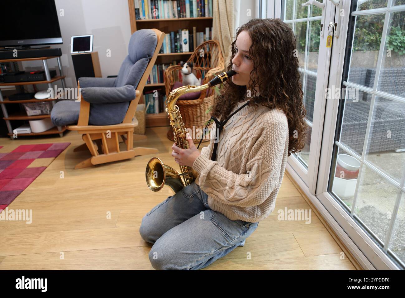 Teenage girl playing saxophone in living room Stock Photo - Alamy