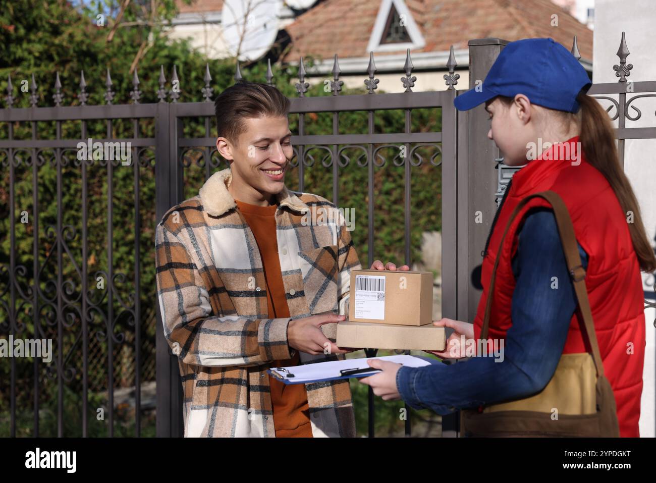 Postwoman giving parcels to young man outdoors Stock Photo - Alamy