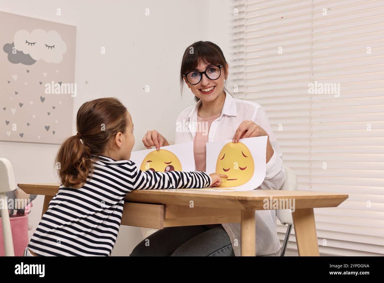 Autism therapy. Little girl choosing emoticon at table with smiling ...