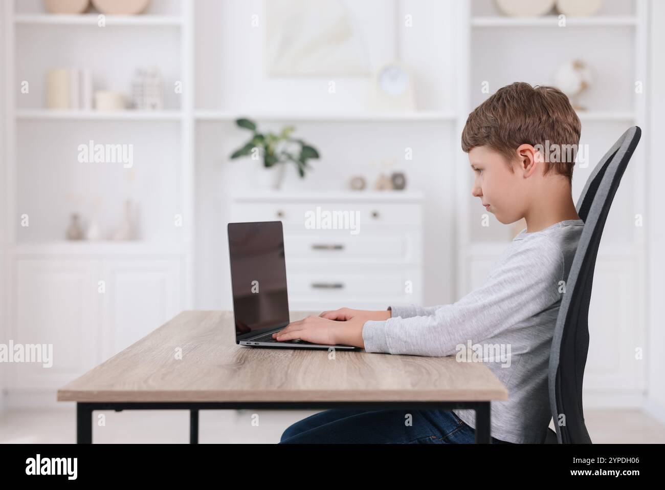 Boy with correct posture using laptop at wooden desk indoors Stock ...