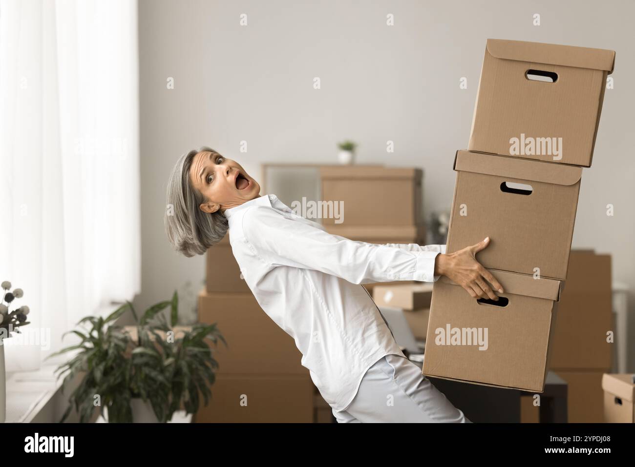 Overwhelmed mature business woman carrying bending stack of heavy boxes ...