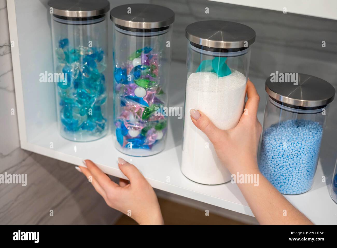 Woman housewife hands putting glass can washing powder laundry capsule ...