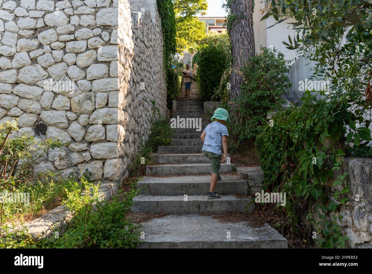 Little boy climbing stone steps surrounded by greenery and rustic walls ...