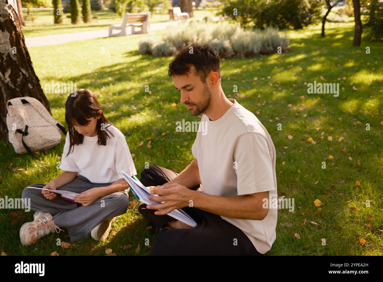 Father and daughter reading books together in a sunny park setting ...