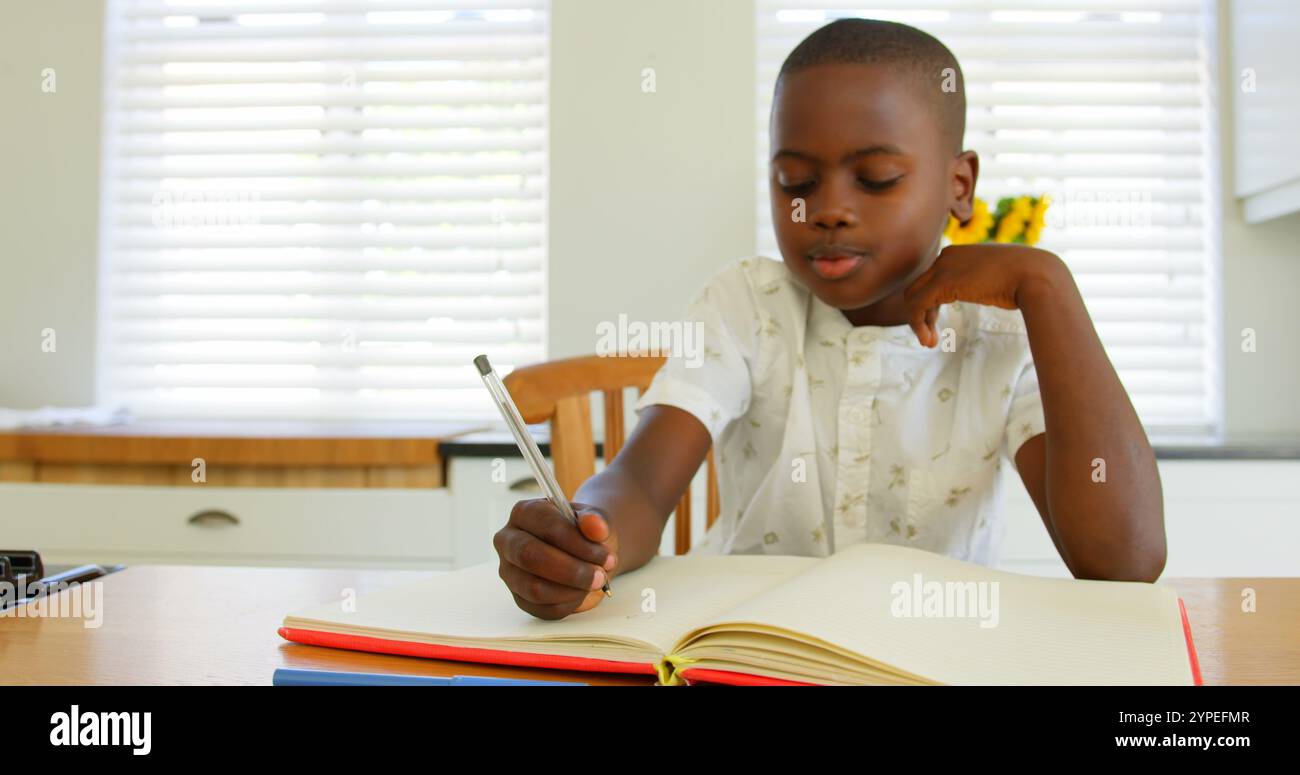 Front view of little black boy doing homework at dining table in a ...