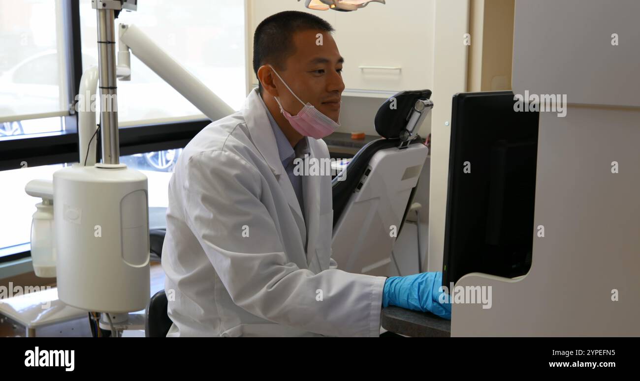 Side view of smiling male Asian dentist wearing white lab coat using ...