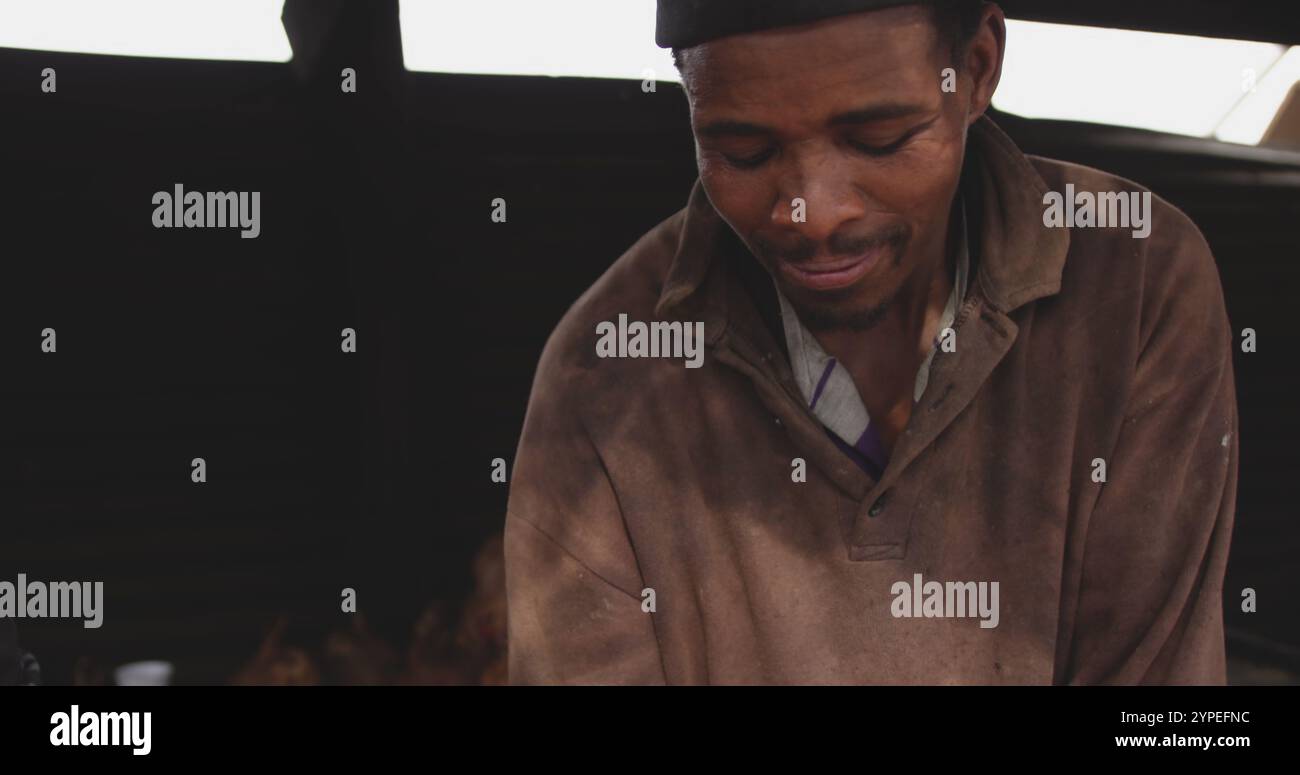 Front view of an African male butcher in a township workshop, holding ...