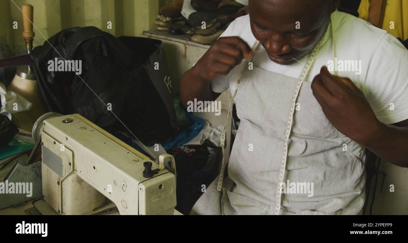Front view of an African male tailor in a township workshop, sitting by ...