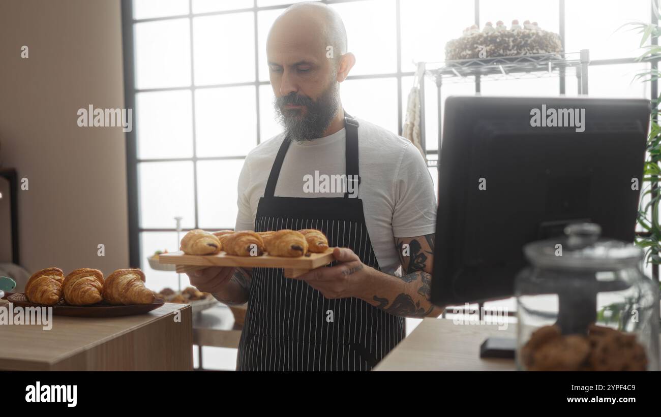 Bald hispanic man holding tray of pastries in indoor bakery shop with ...
