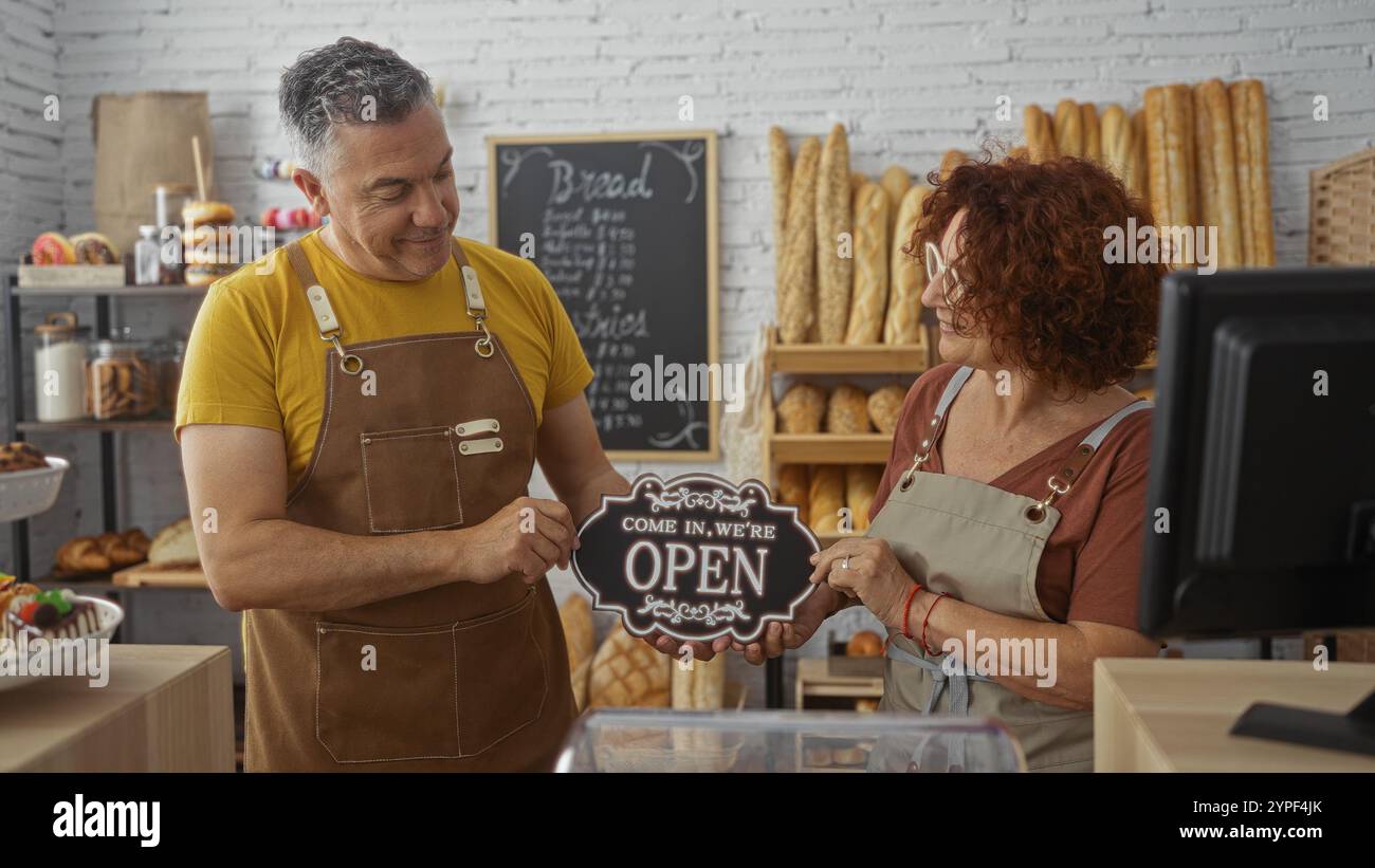 Bakers holding open sign inside bakery with shelves of bread and ...