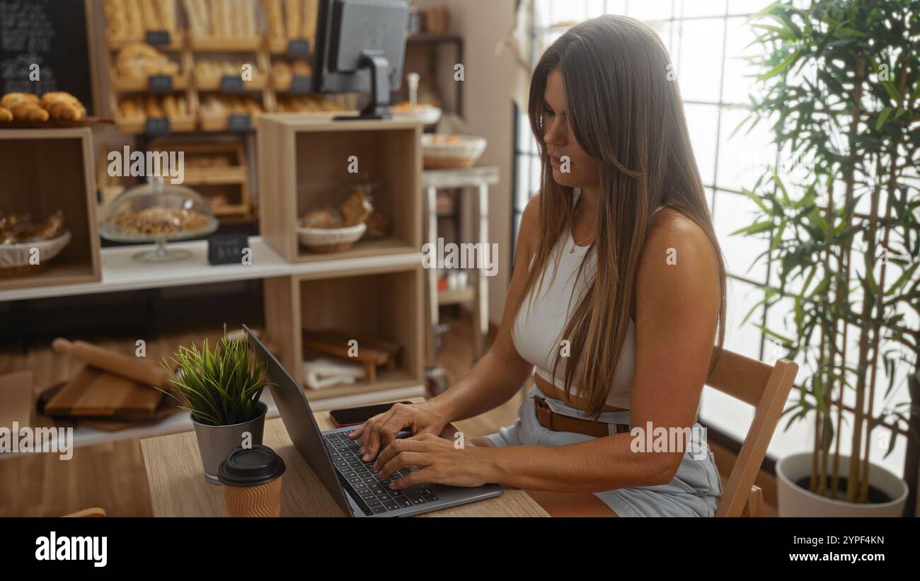Woman typing indoors at bakery with laptop and coffee surrounded by ...