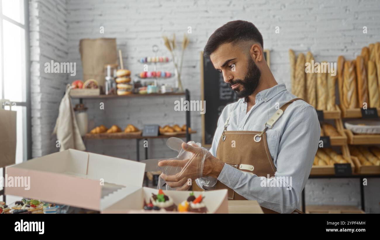 Young hispanic man with a beard working in a bakery shop, wearing an ...