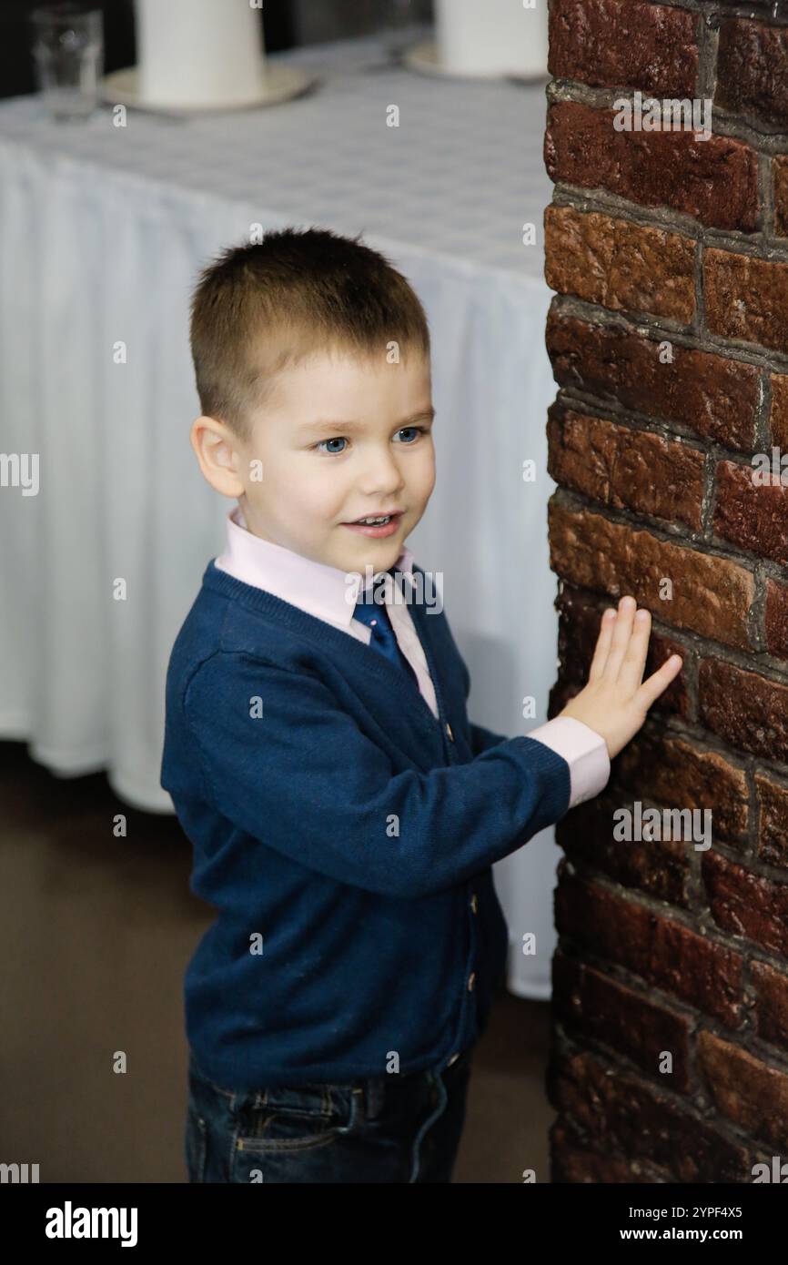 Young boy dressed in elegant attire, touching a brick wall, exploring ...