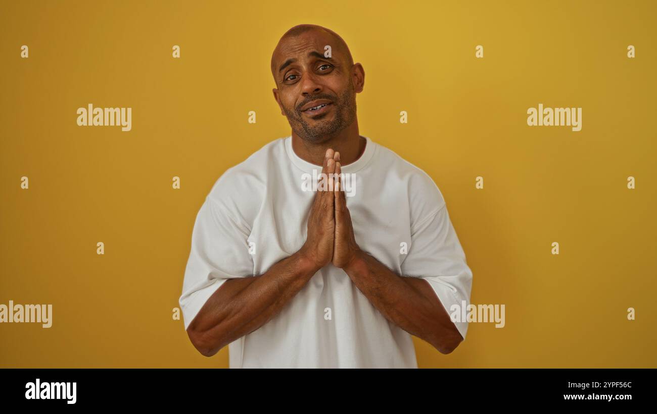 Young man making a plea gesture with hands together, standing against ...