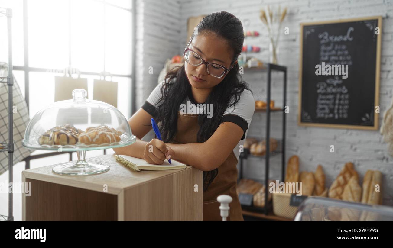 Young chinese woman jotting down notes in a cozy bakery interior with ...