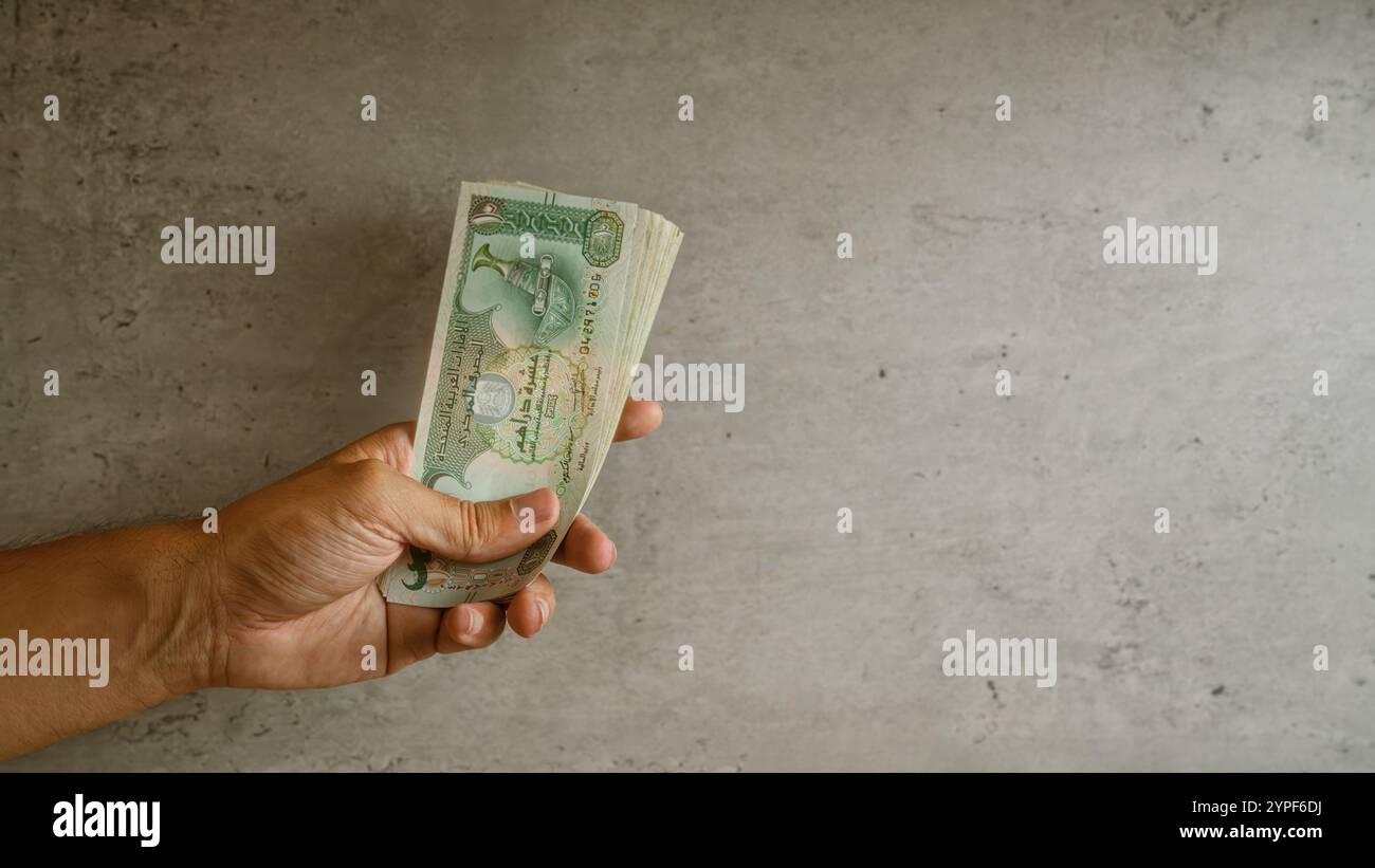 Hand holding uae dirham banknotes against a concrete background ...