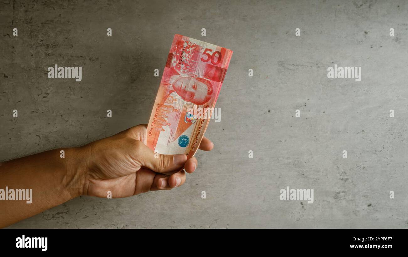 Hand holding a philippine peso bill against a concrete background ...