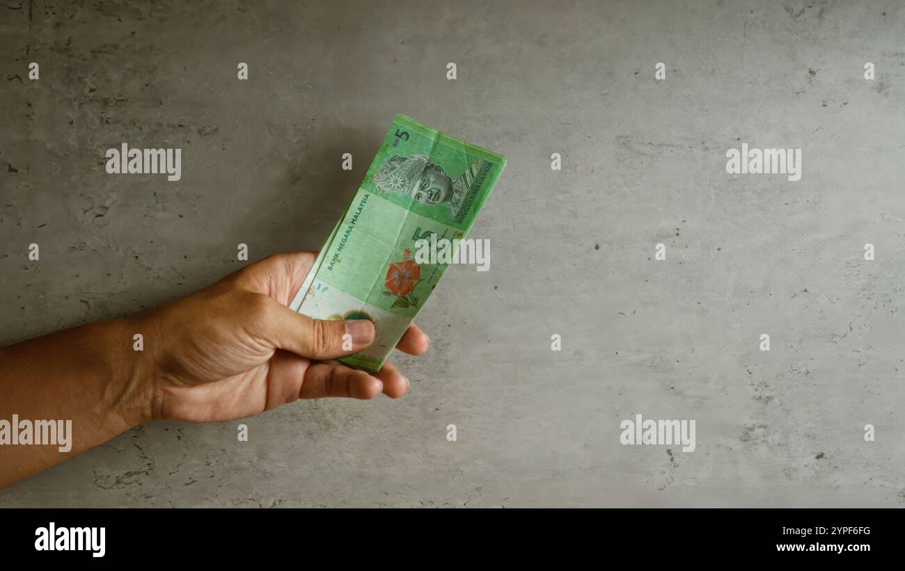 Man holding a 5 malaysian ringgit note against a concrete background ...