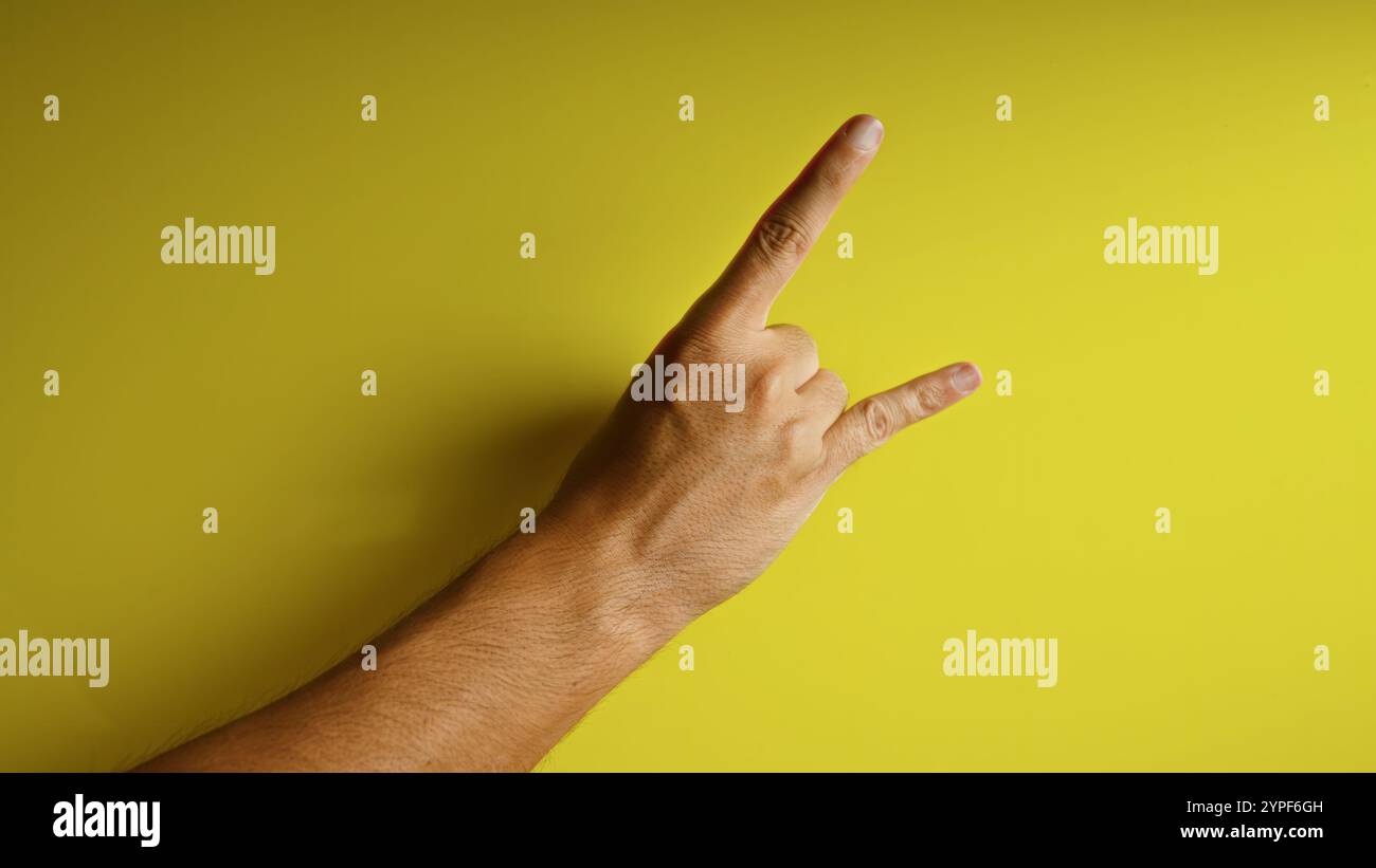 Man's hand making a rock on gesture over a bright yellow background ...