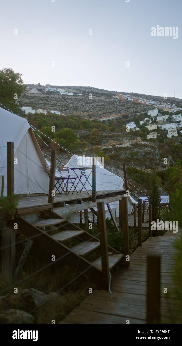 A row of white tents lined up along a raised wooden walkway in a scenic ...