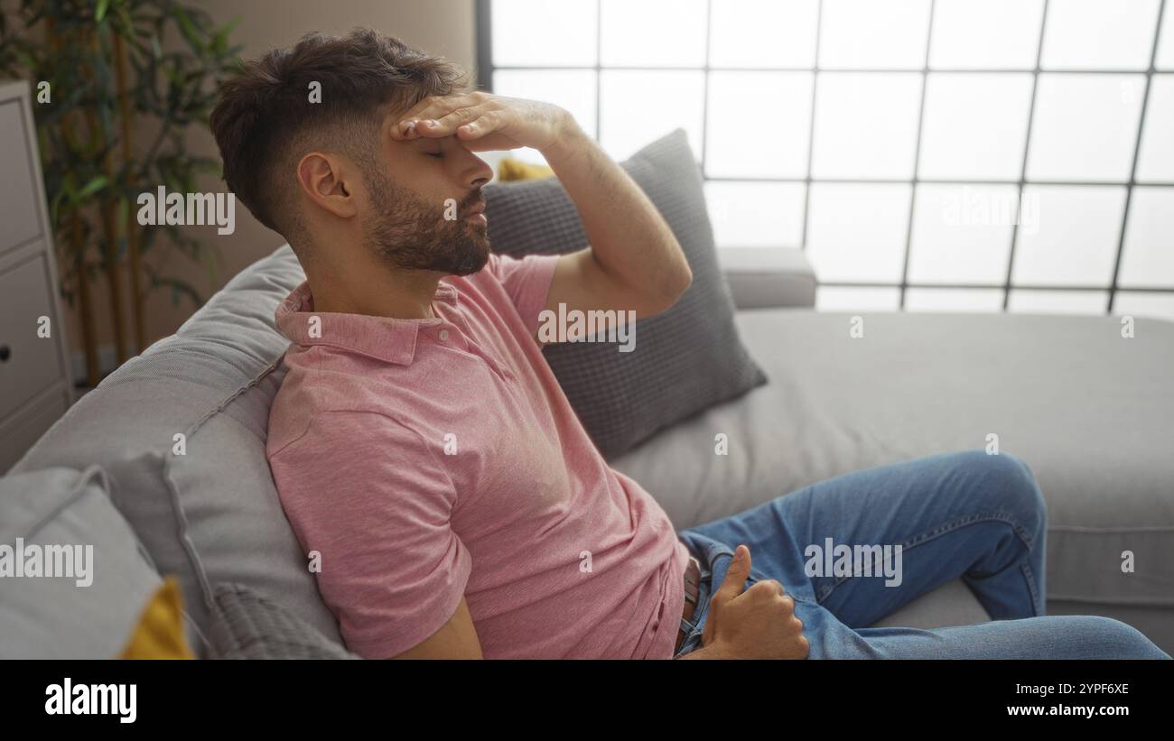 Young man with a beard looks stressed while sitting on a couch in a ...