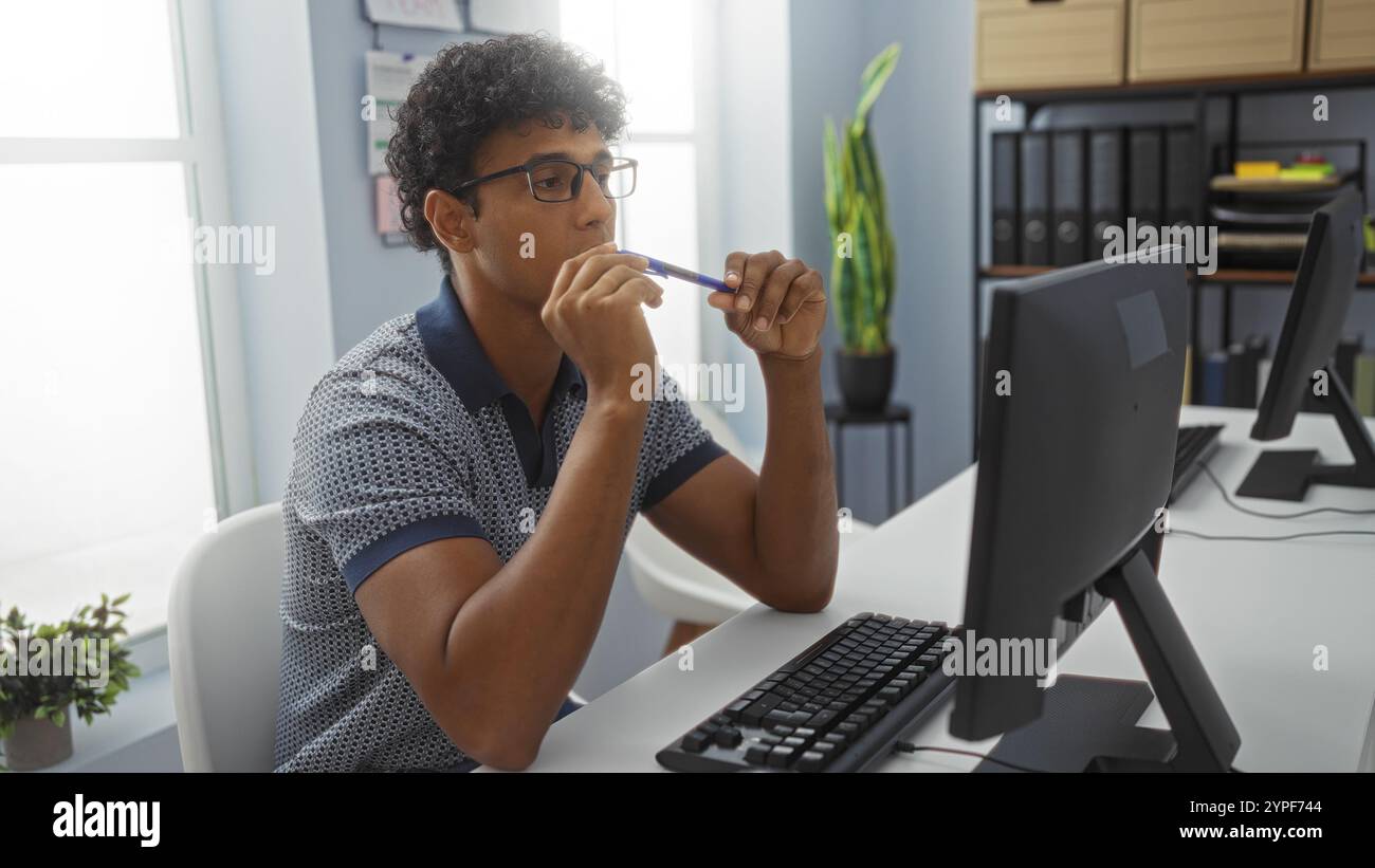Young man thinking while working at a computer in an office setting ...