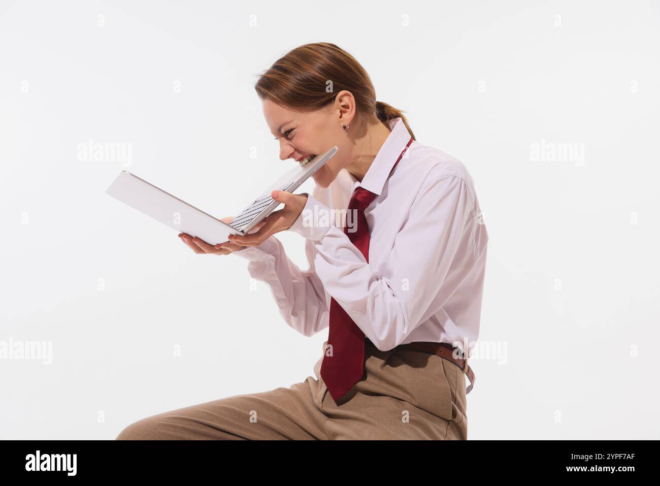 Stylish young woman in white shirt and red tie bites her laptop in ...