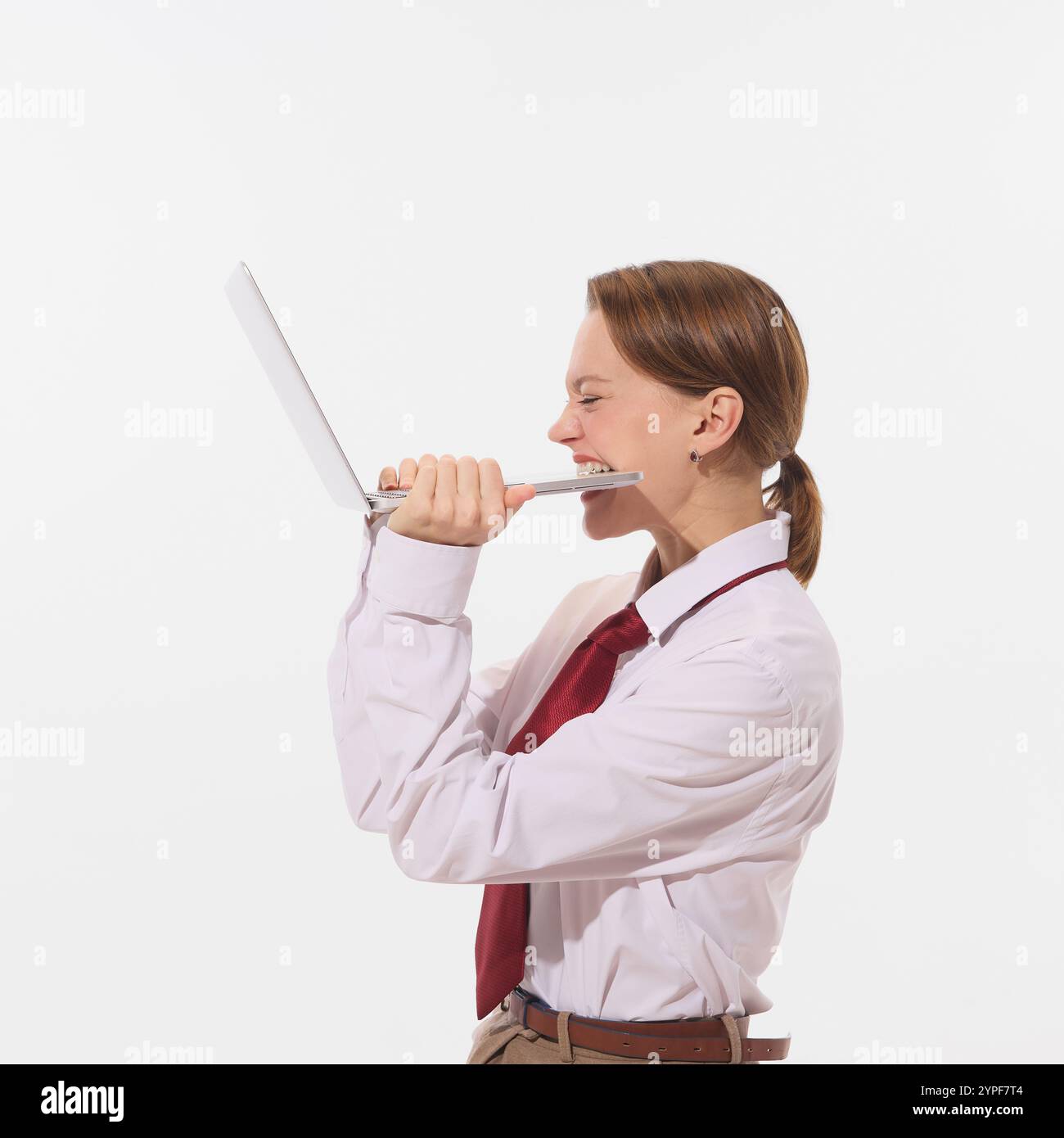 Young woman dressed in office attire angrily bites her laptop ...