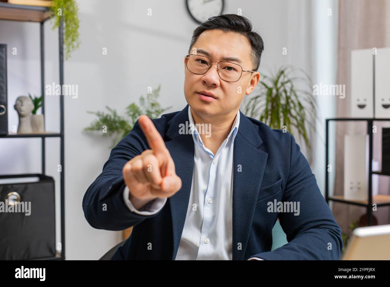 Asian middle-aged businessman working on laptop computer shakes finger ...