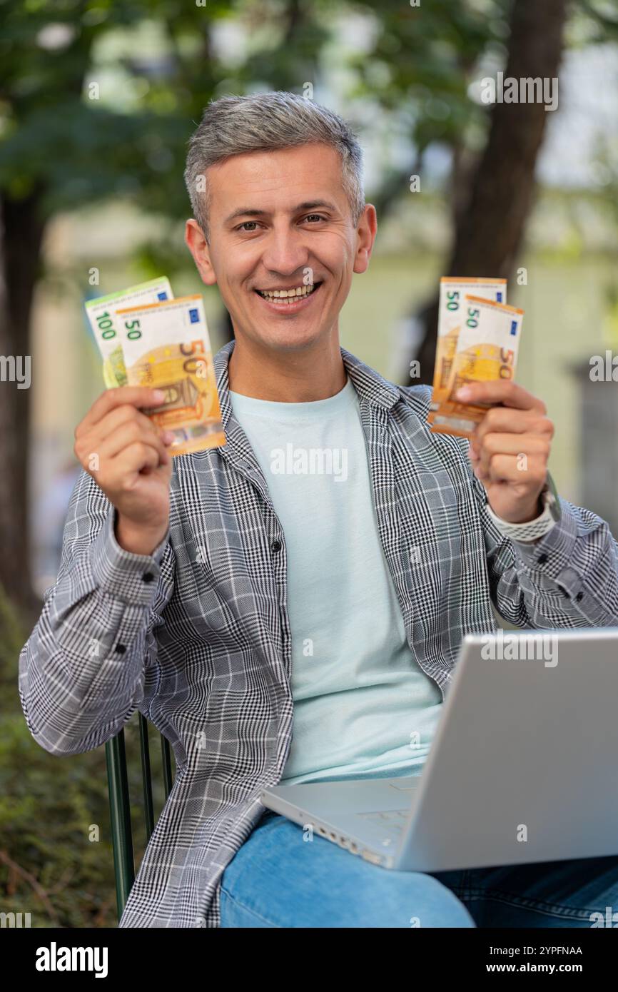 Happy rich man using laptop winner victory counting holding fan of cash ...