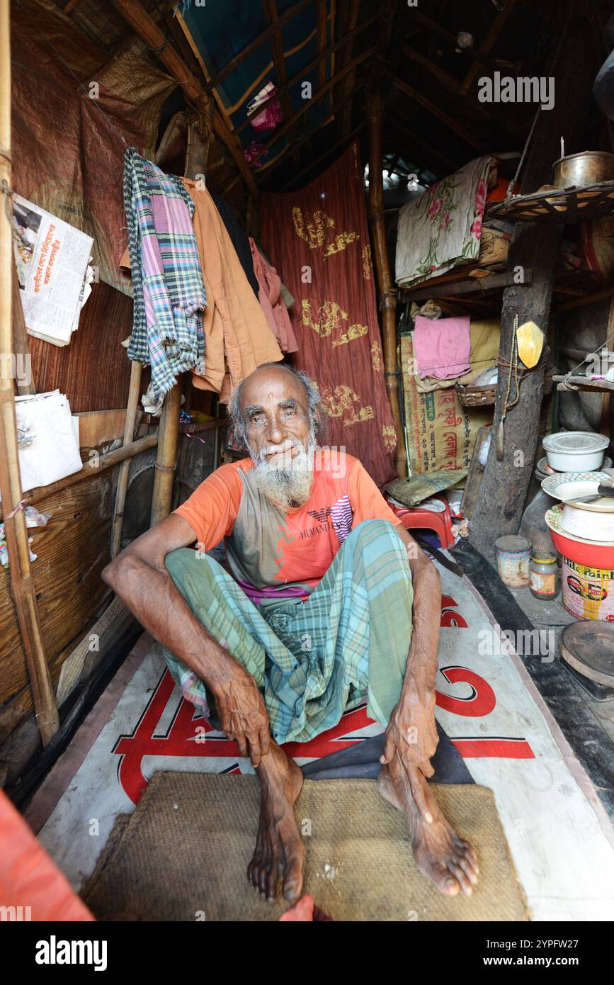 A Bengali man sitting in his tiny home in a roadside slum in Dhaka ...