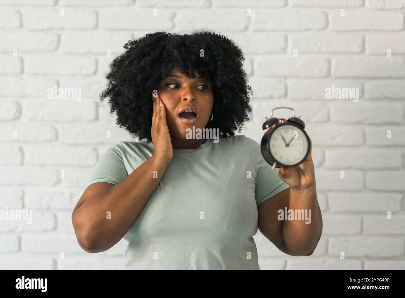 Surprised African American woman holding an alarm clock while ...