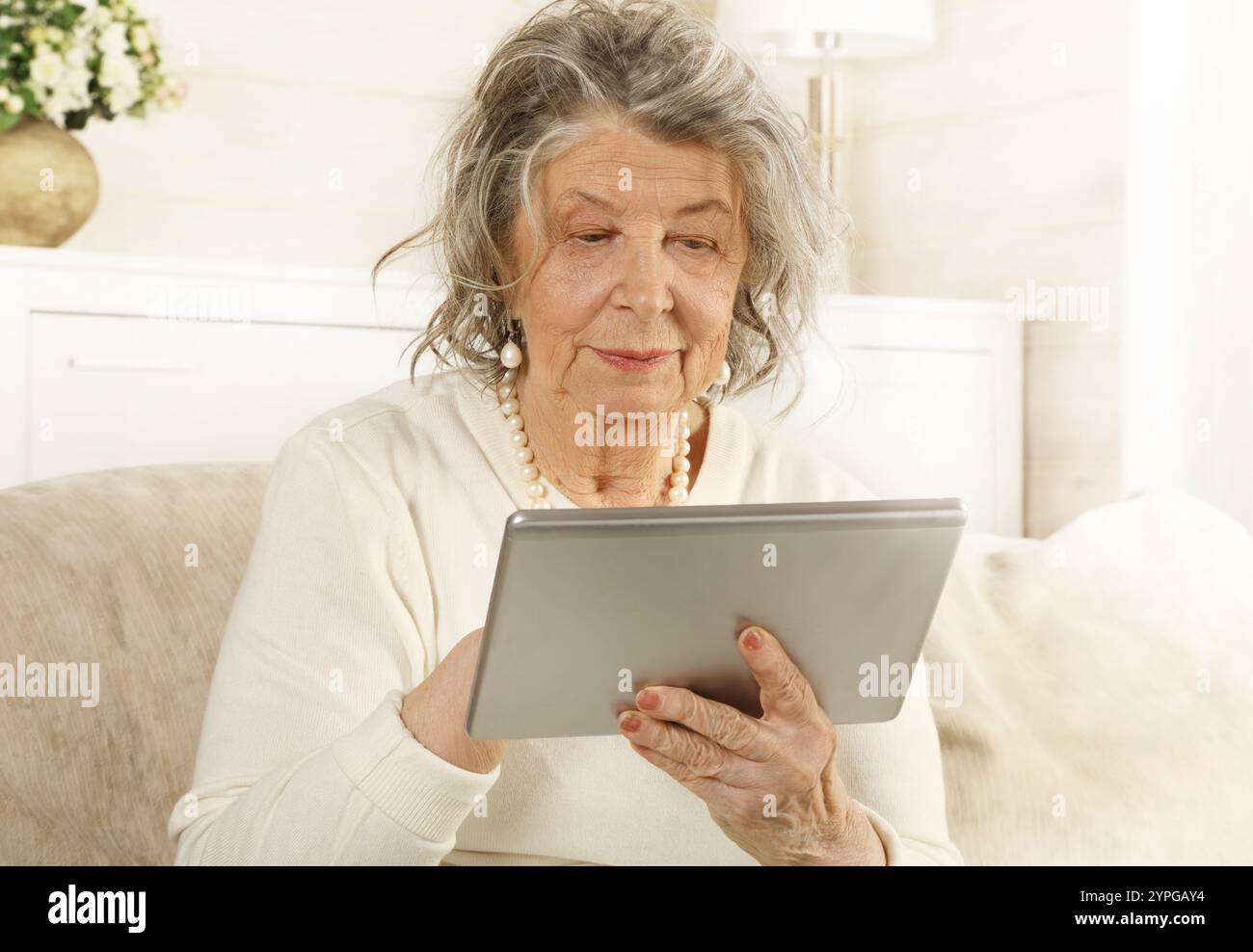 An old lady is working with a tablet computer sitting on the sofa in ...