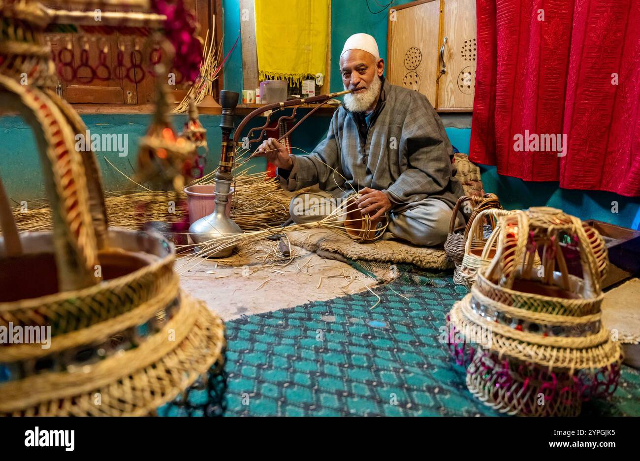 Ali Mohammad Dar, an artisan, smokes hookah as he designs a "Kangri" (a ...