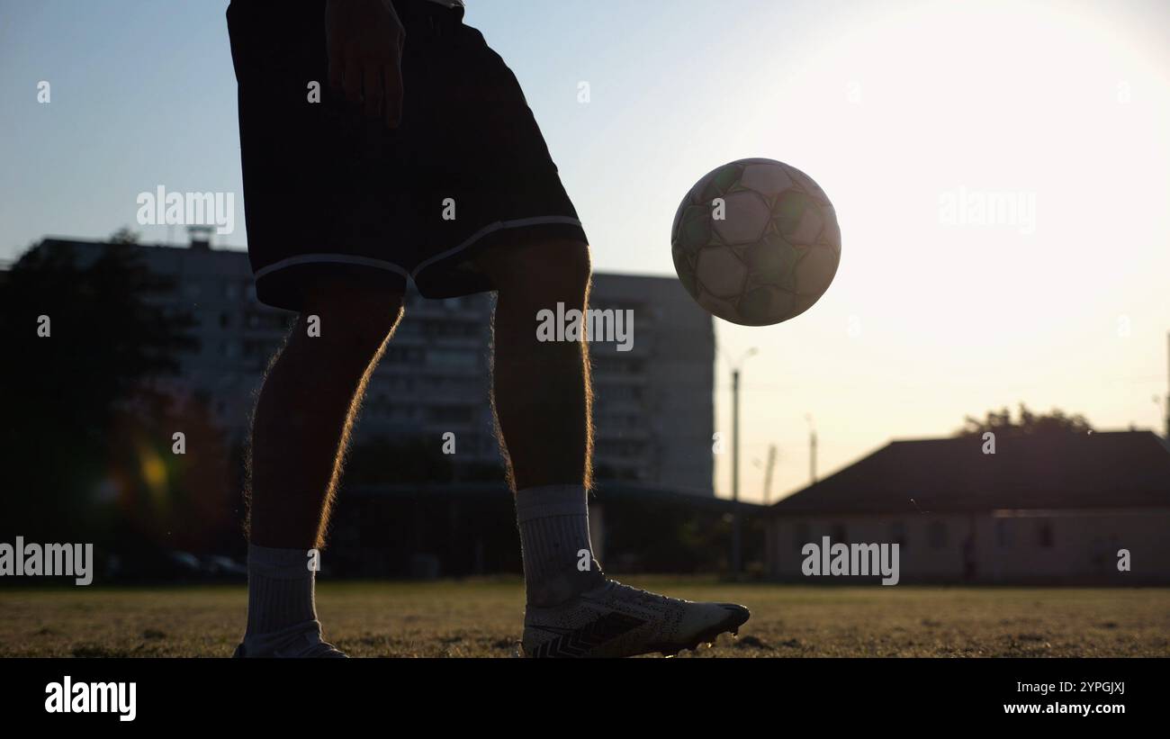 Legs of young man kicking ball at green field. Male feet of ...