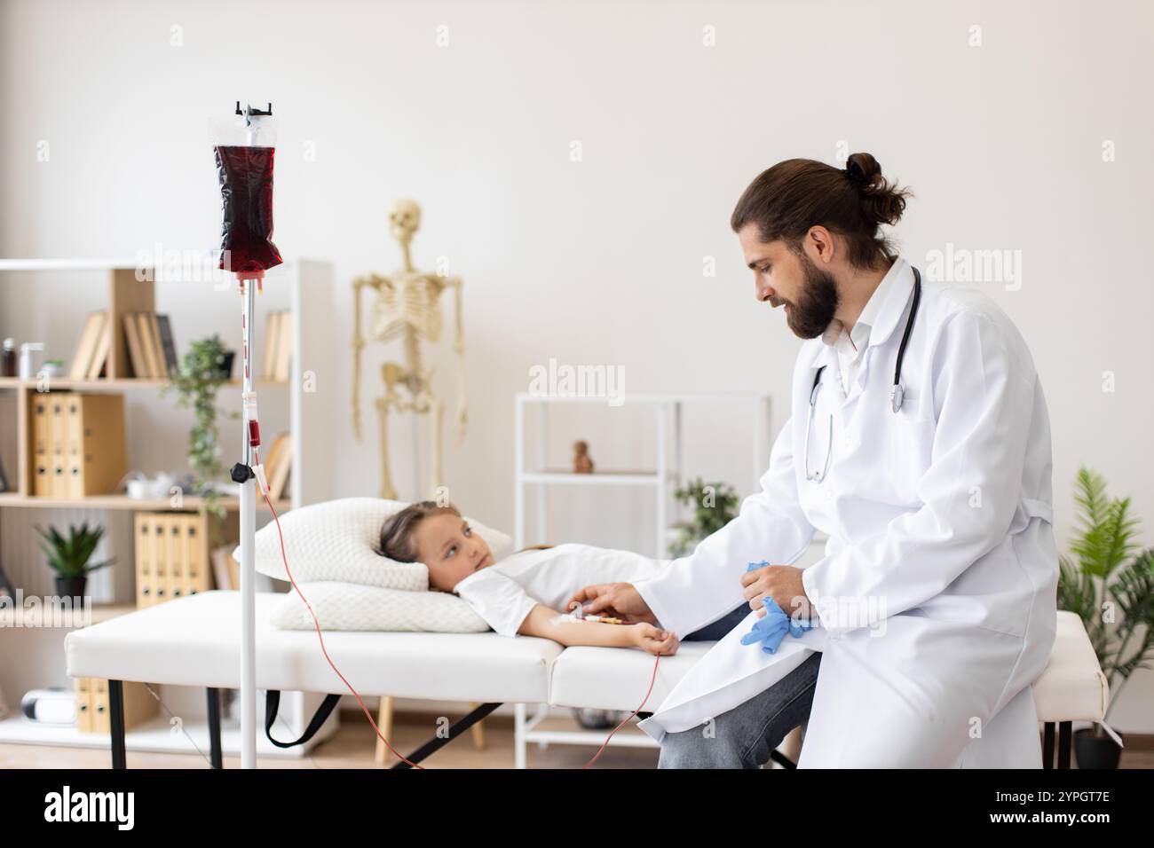 Male doctor assists young Caucasian girl receiving blood transfusion at ...