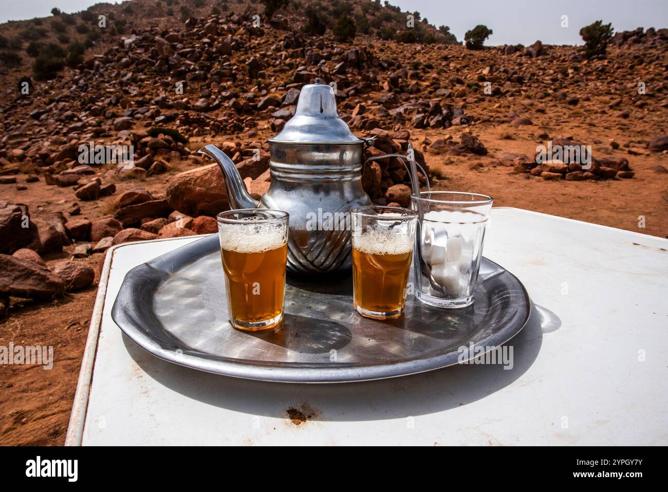 three glasses of Moroccan tea with iron teapot on tray in the desert ...