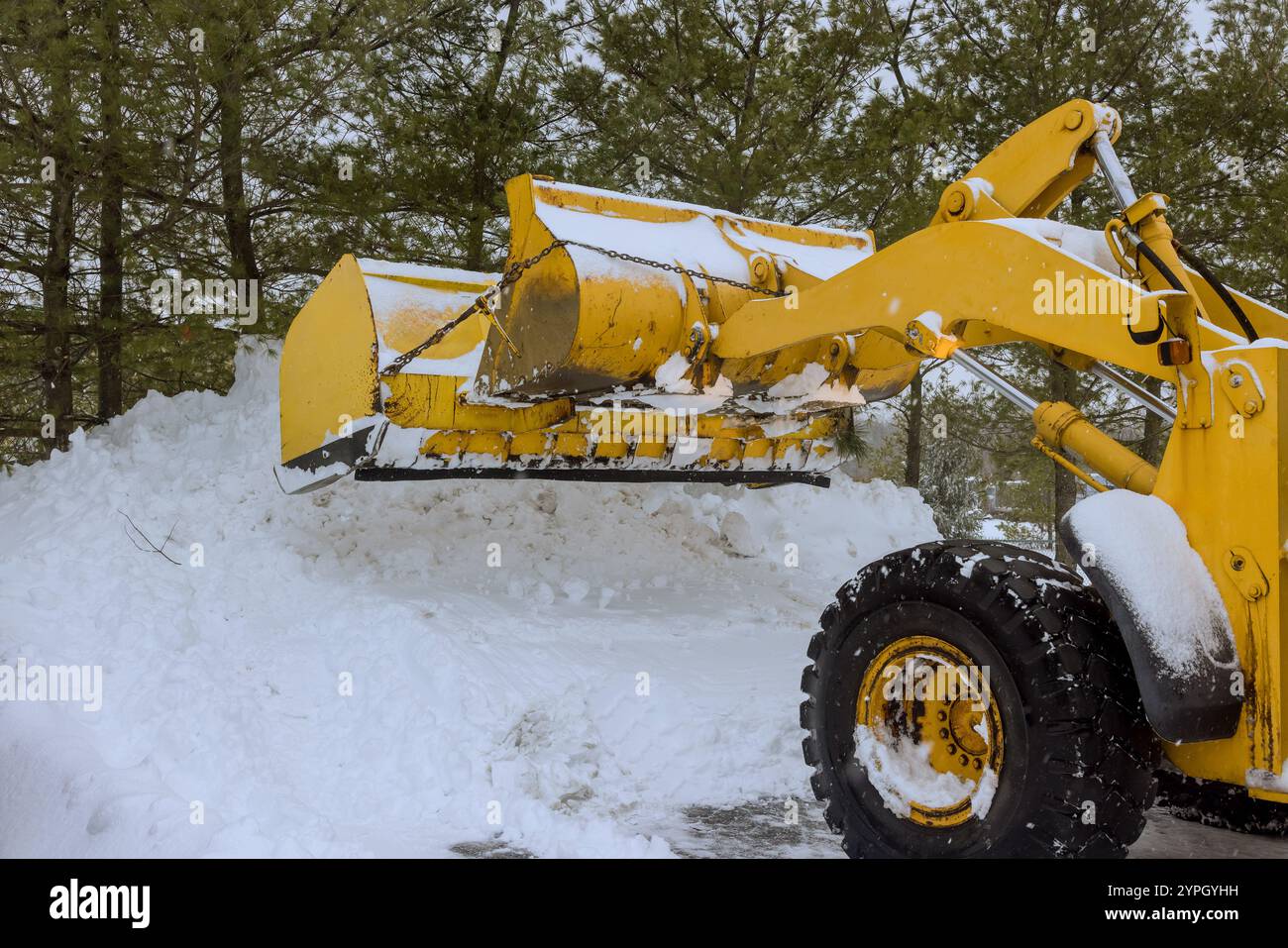 Heavy machinery works to remove thick snow buildup from driveway during ...